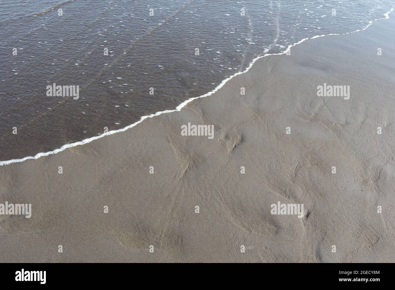 Sandy gray seashore with the ocean wave coming towards a it viewed from ...