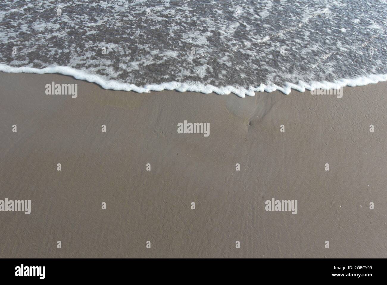 Sandy gray seashore with the ocean wave coming towards a it viewed from ...