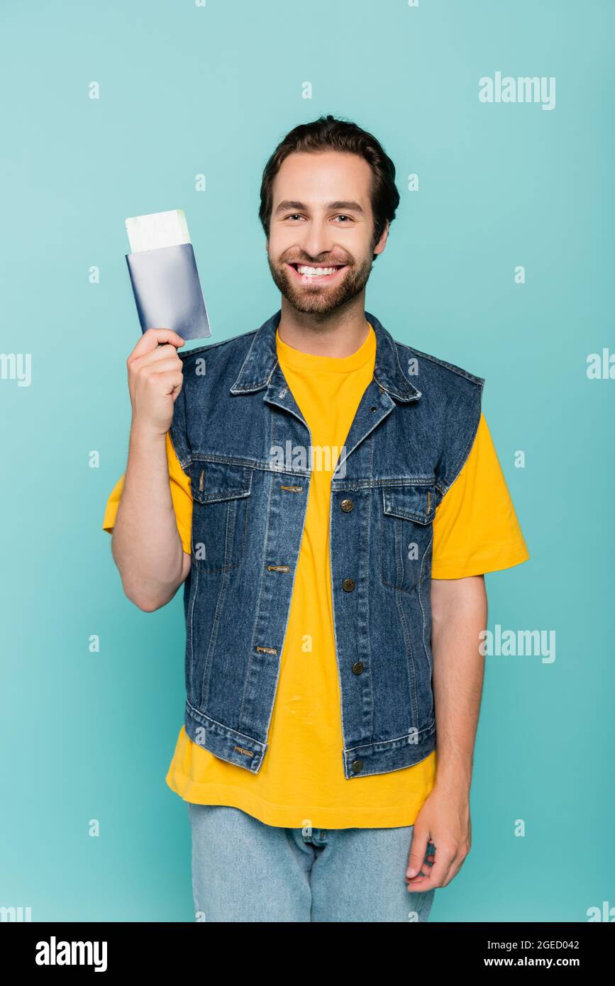 Brunette man with passport and boarding pass smiling at camera isolated ...