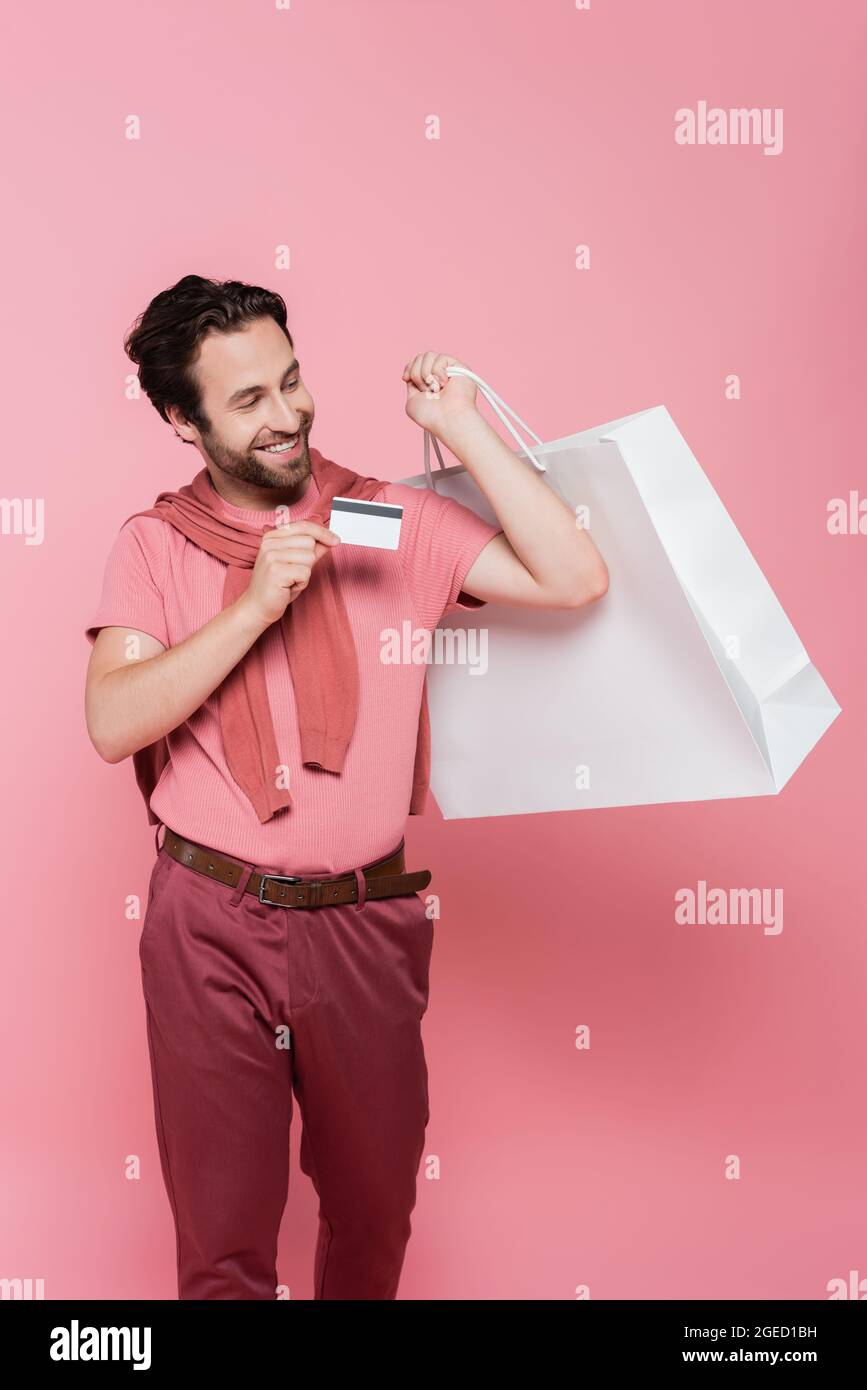 Brunette shopaholic holding shopping bag and credit card on pink ...