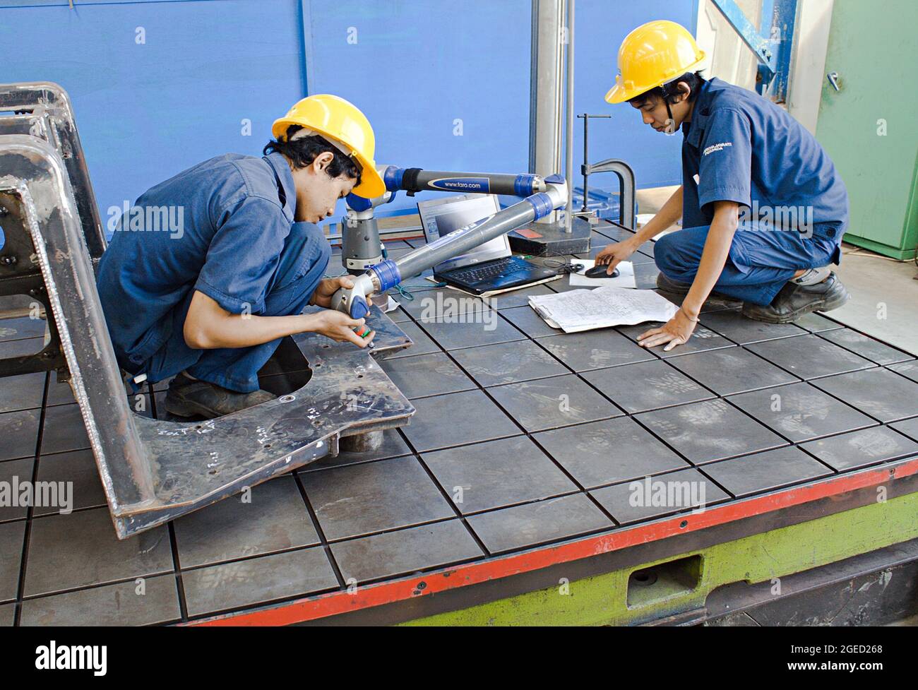 Two technicians use measurement tool and laptop in a metal fabrication ...