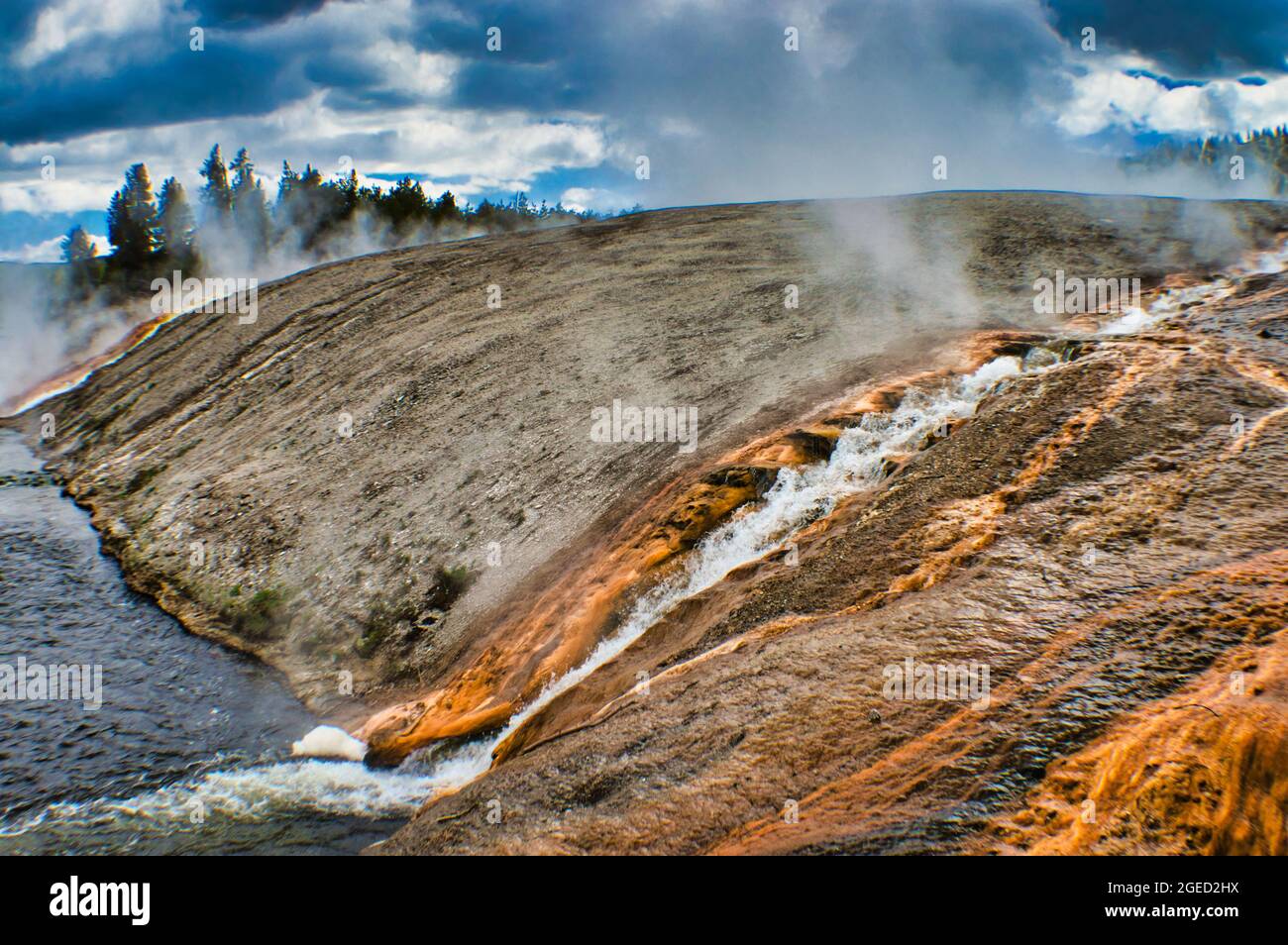 Steamy geyser waterfall flowing from rock into a basin near forest ...