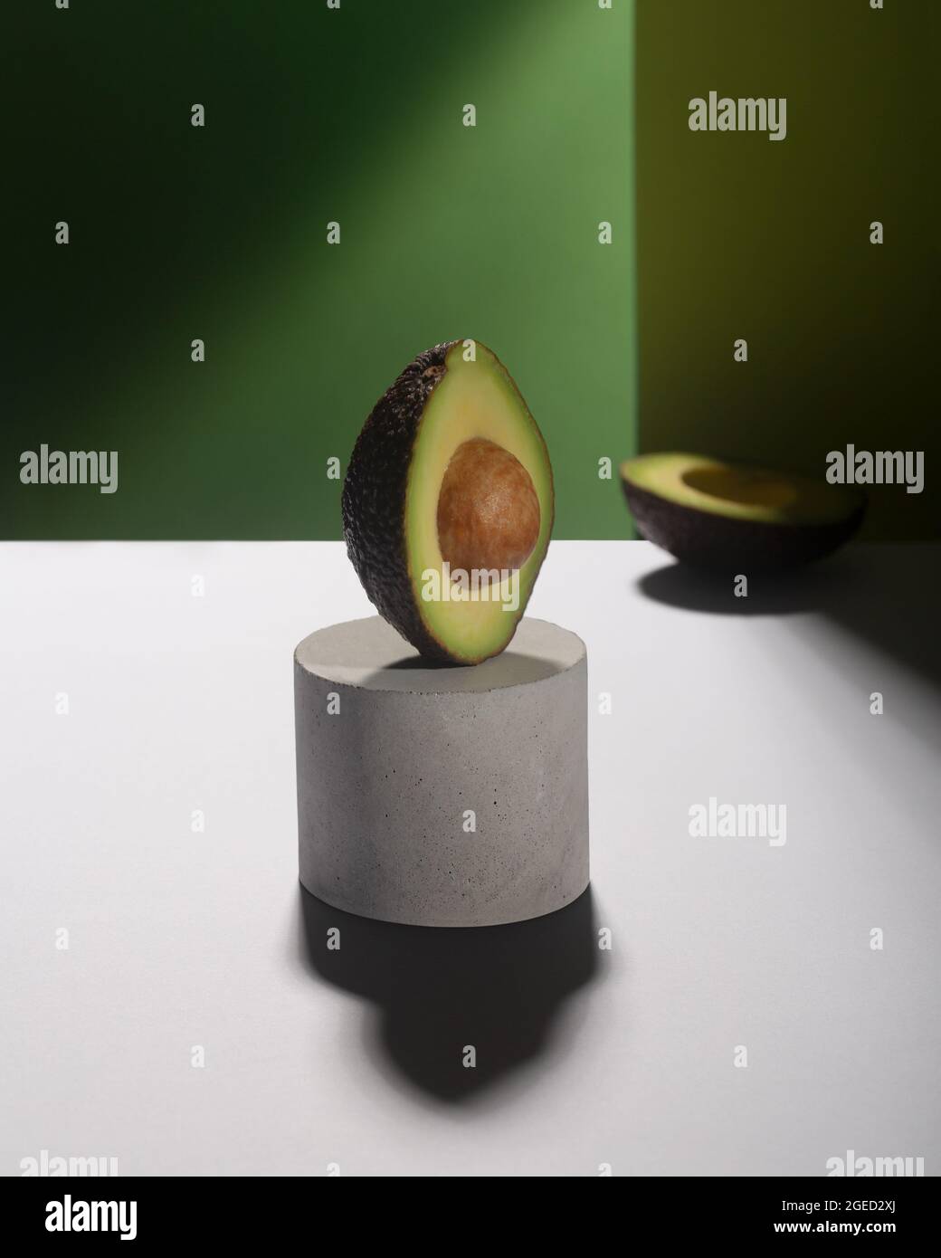 Creative avocado balance on the concrete stand, green background ...