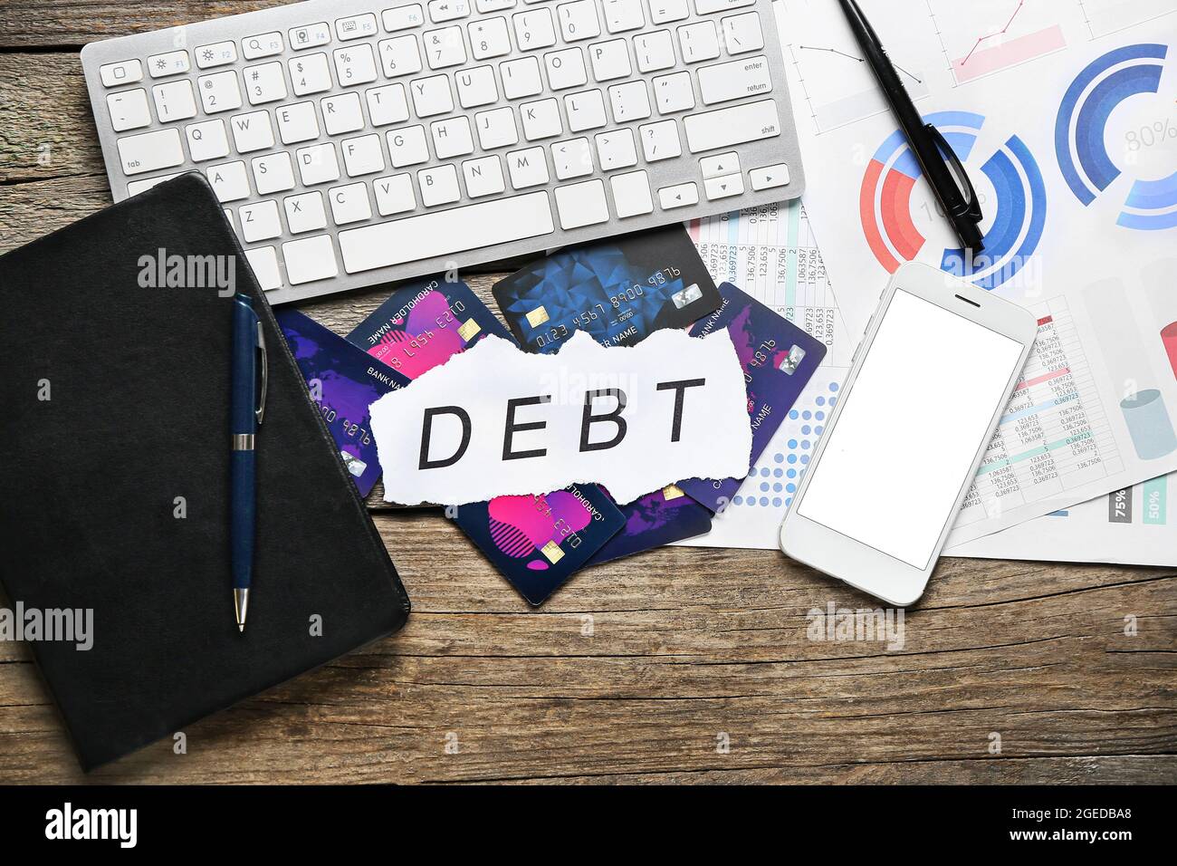 Paper with word DEBT, credit cards and gadgets on wooden background ...