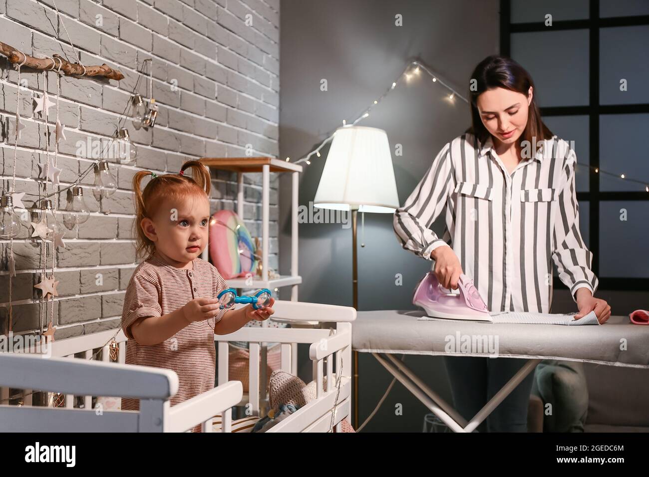 Mother with little baby ironing clothes at home late in evening Stock ...
