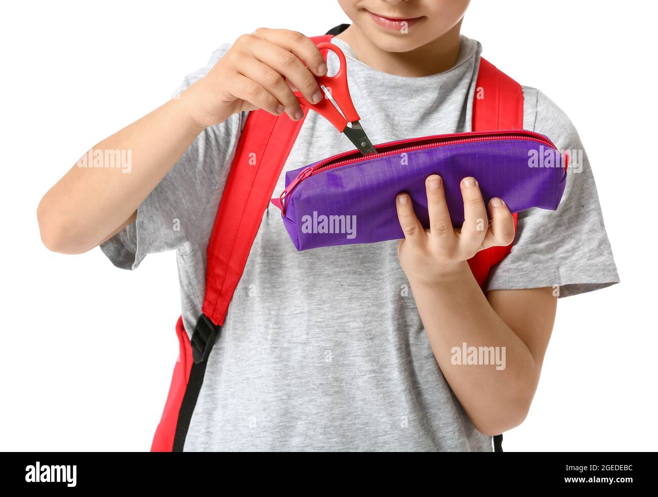 Little schoolboy putting scissors in pencil case on white background ...