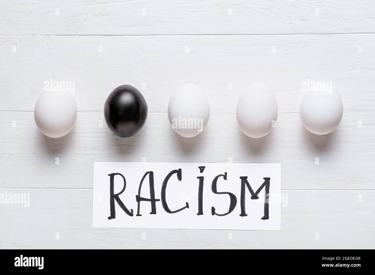 Different eggs on white wooden background. Racism concept Stock Photo ...