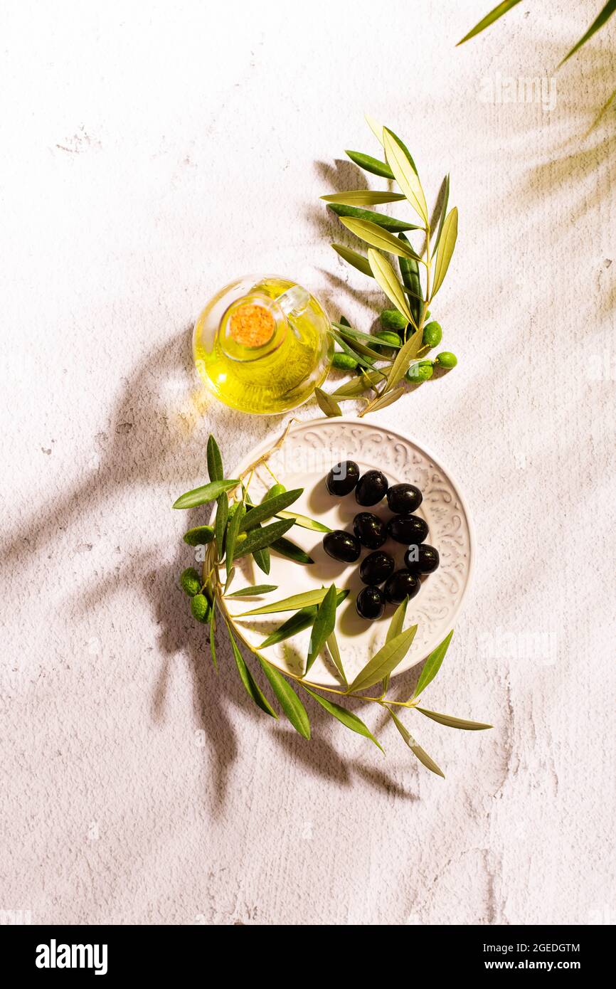 A glass jar with virgin olive oil, textured plate with black olives and ...