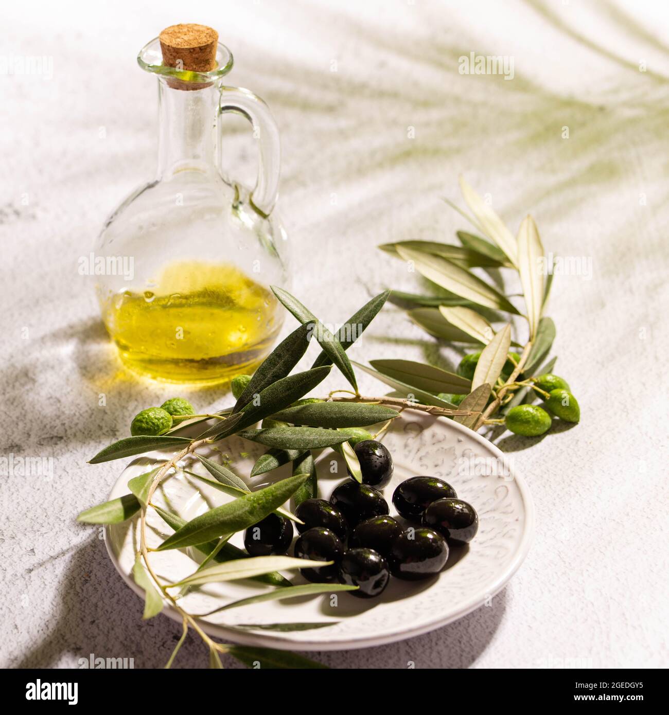 A glass jar with virgin olive oil, textured plate with black olives and ...