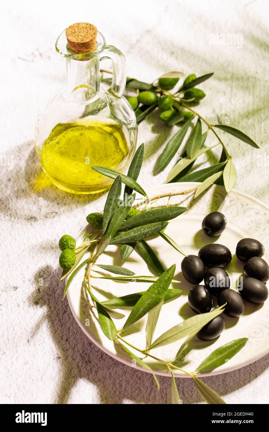 A glass jar with virgin olive oil, textured plate with black olives and ...