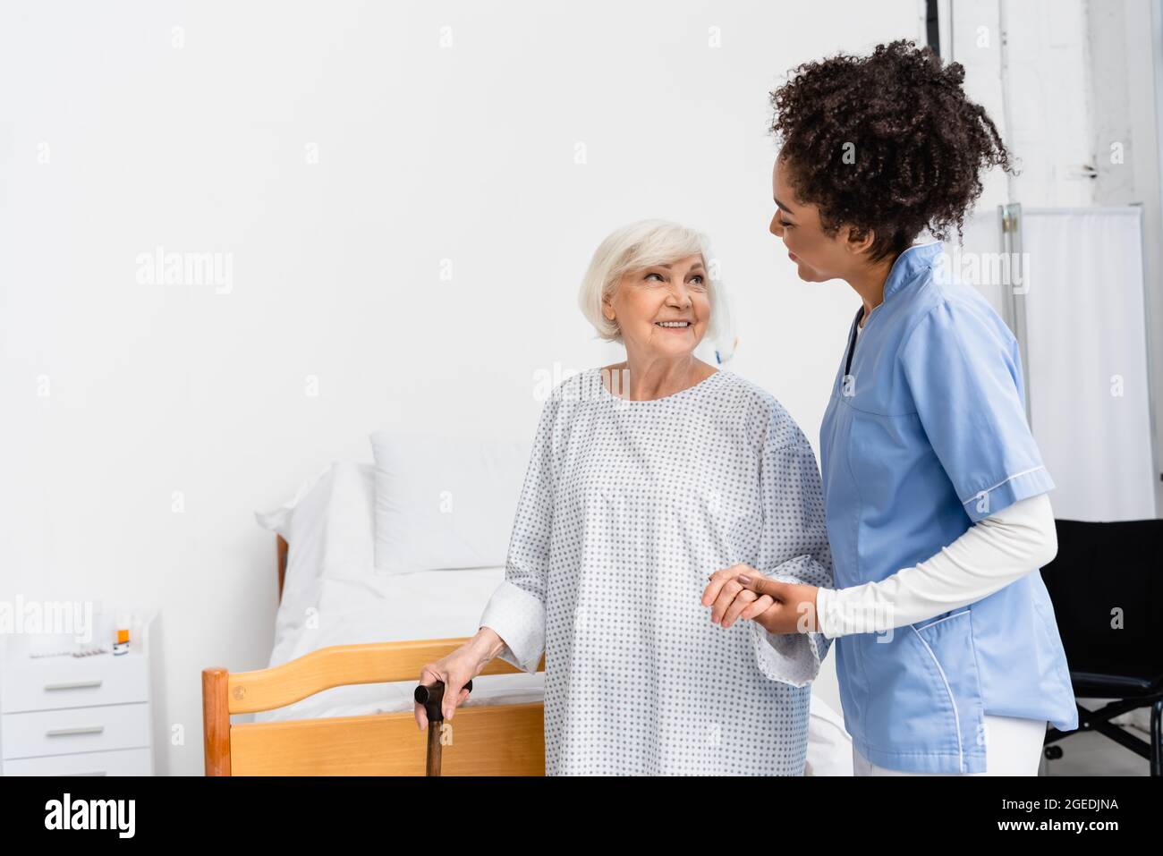 Cheerful elderly woman with walking cane holding hand of african ...