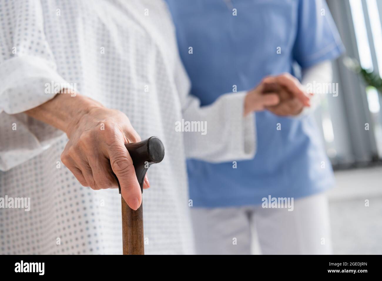 Cropped view of senior patient holding walking cane near blurred nurse ...
