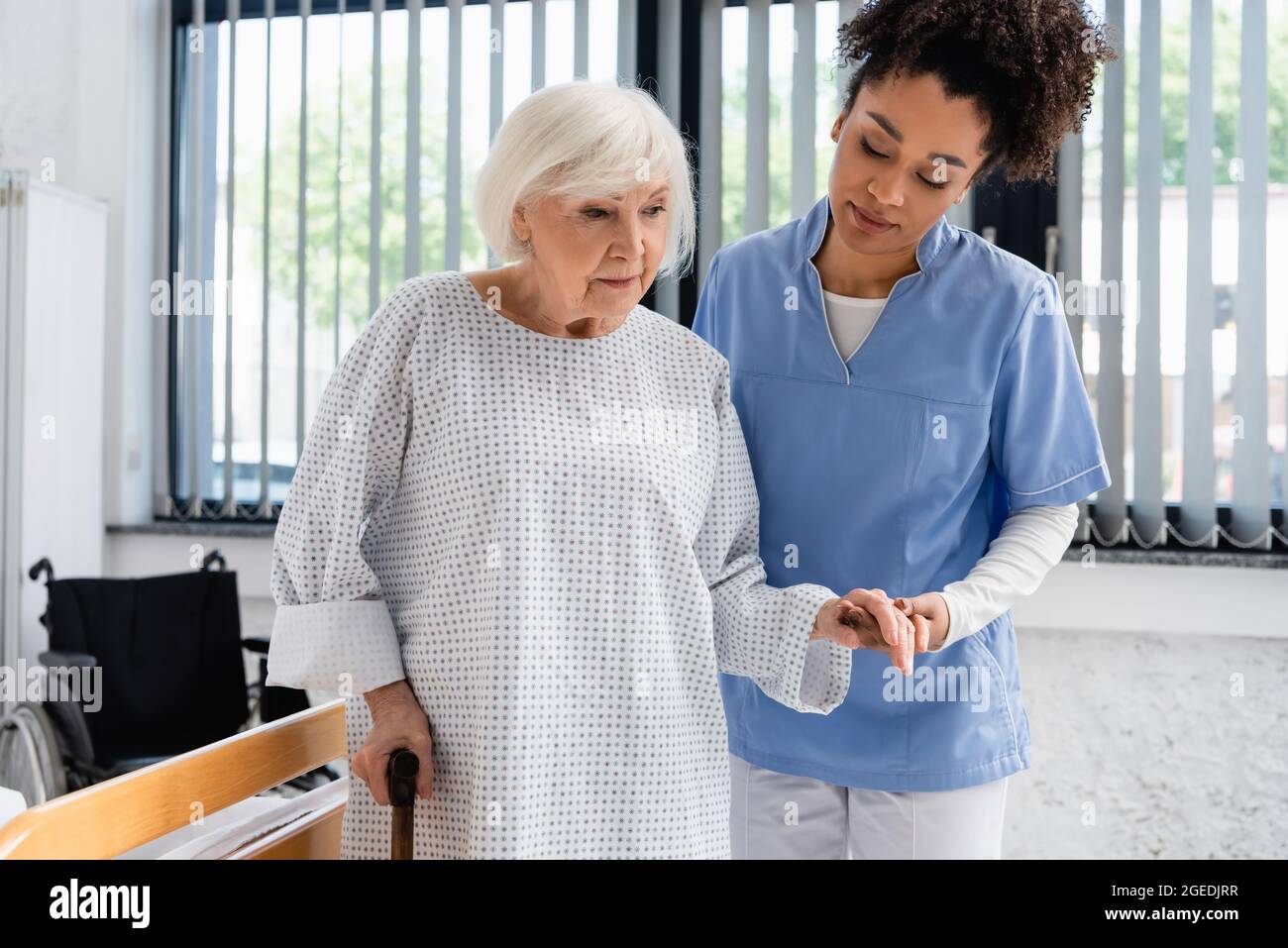 African american nurse holding hand of patient with walking cane in ...