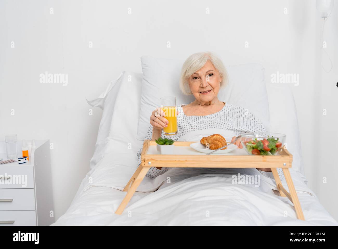 Senior patient holding orange juice near food on tray in hospital ward ...
