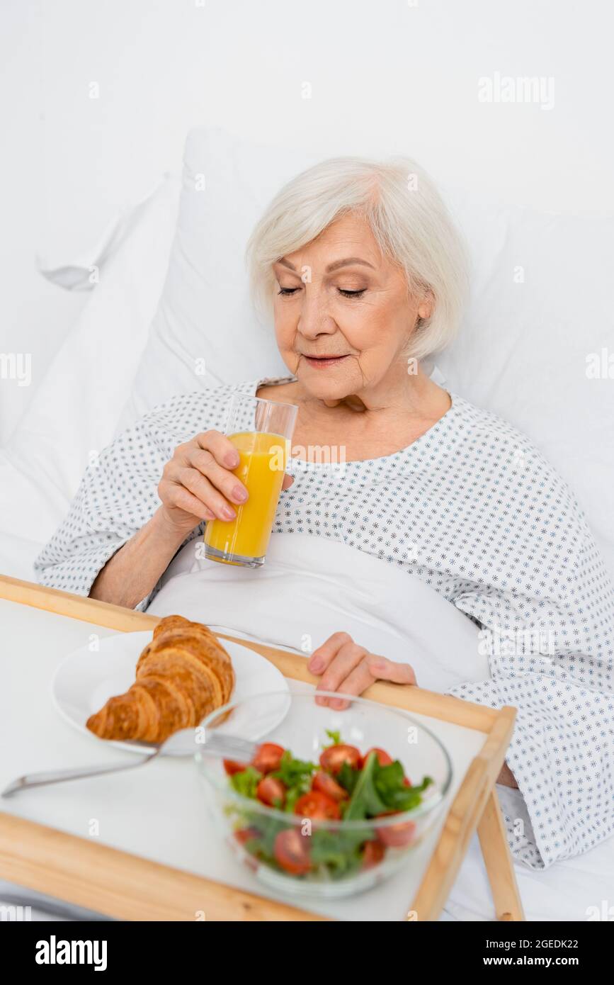 Elderly woman holding glass of orange juice near food on tray on ...