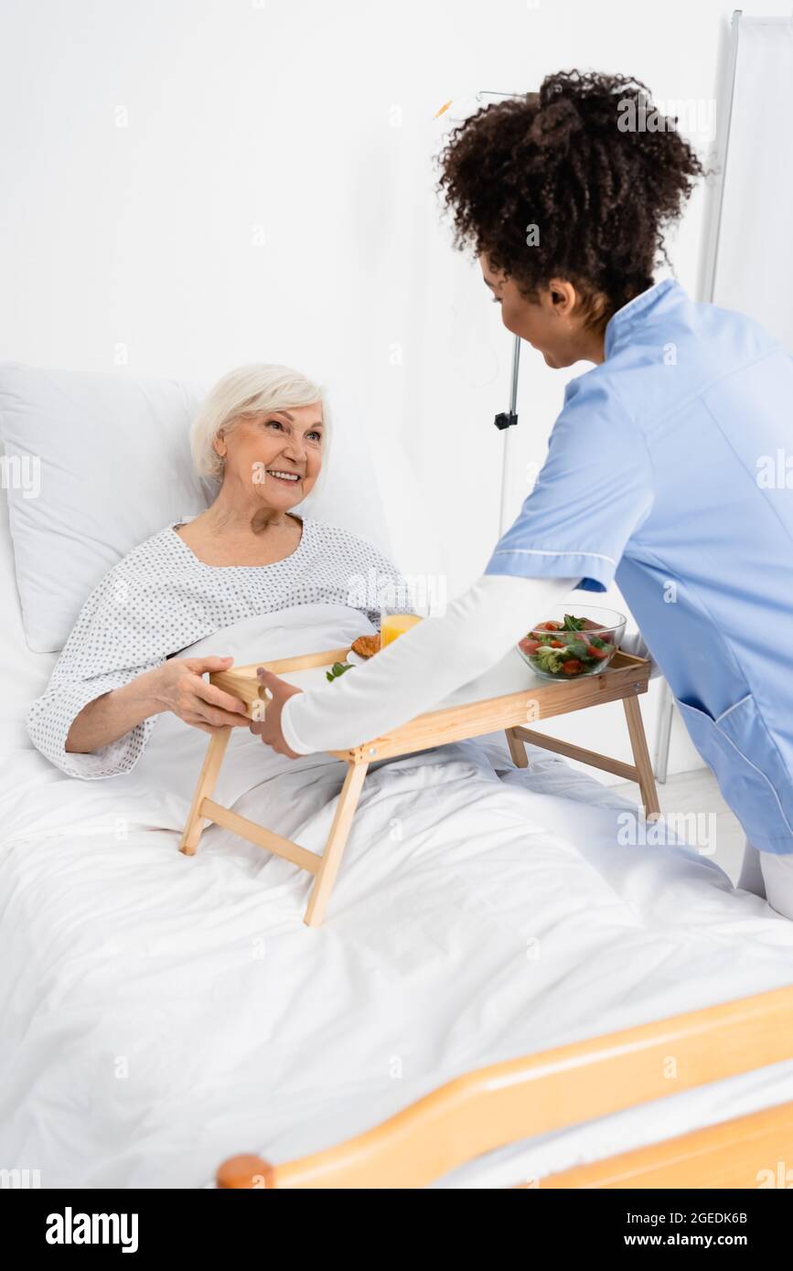 African american nurse holding tray with food near cheerful patient on ...