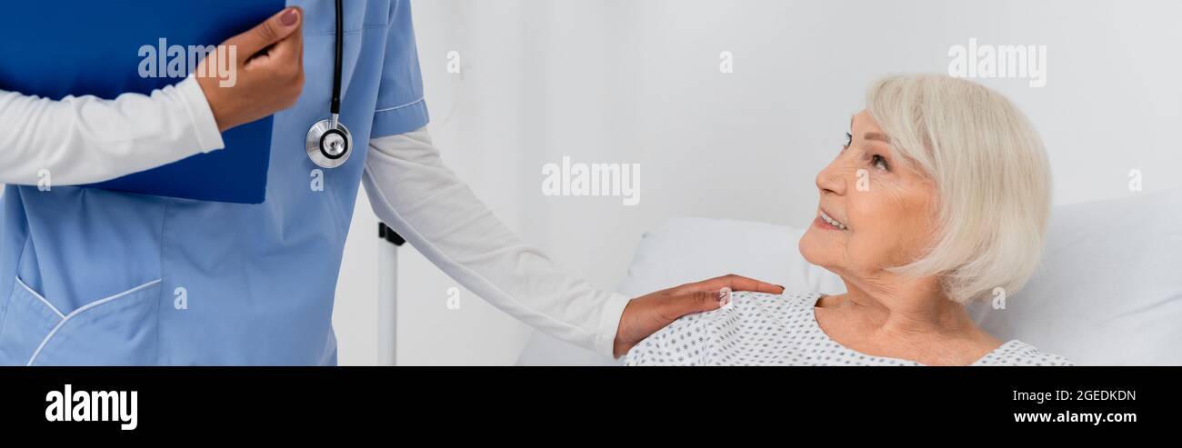 African american nurse with clipboard touching smiling senior patient ...