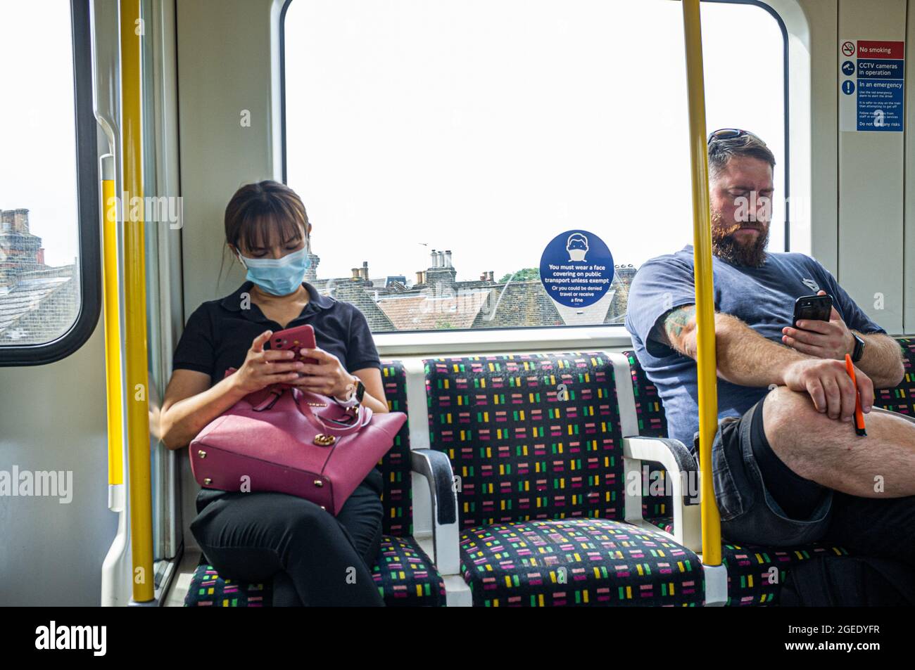 WIMBLEDON LONDON 19 August 2021. Two passengers sitting in contrast to ...