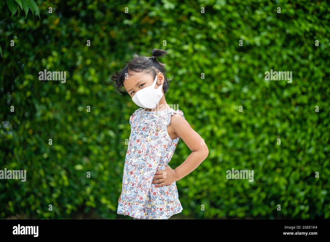Beautiful Southeast Asian female kid with a mask on her face standing ...