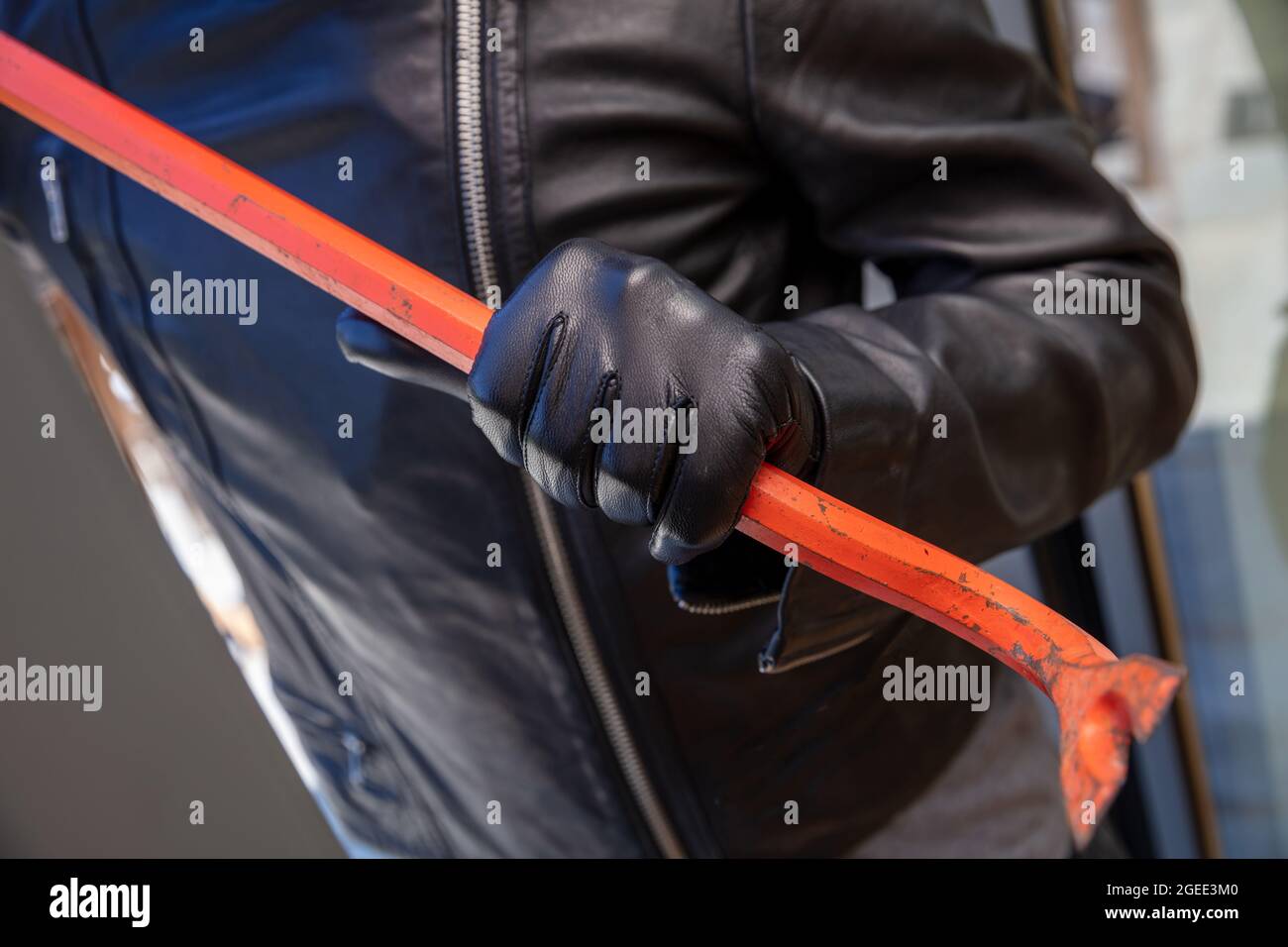 Burglar in leather jacket breaking a glass aluminum door. Masked thief ...