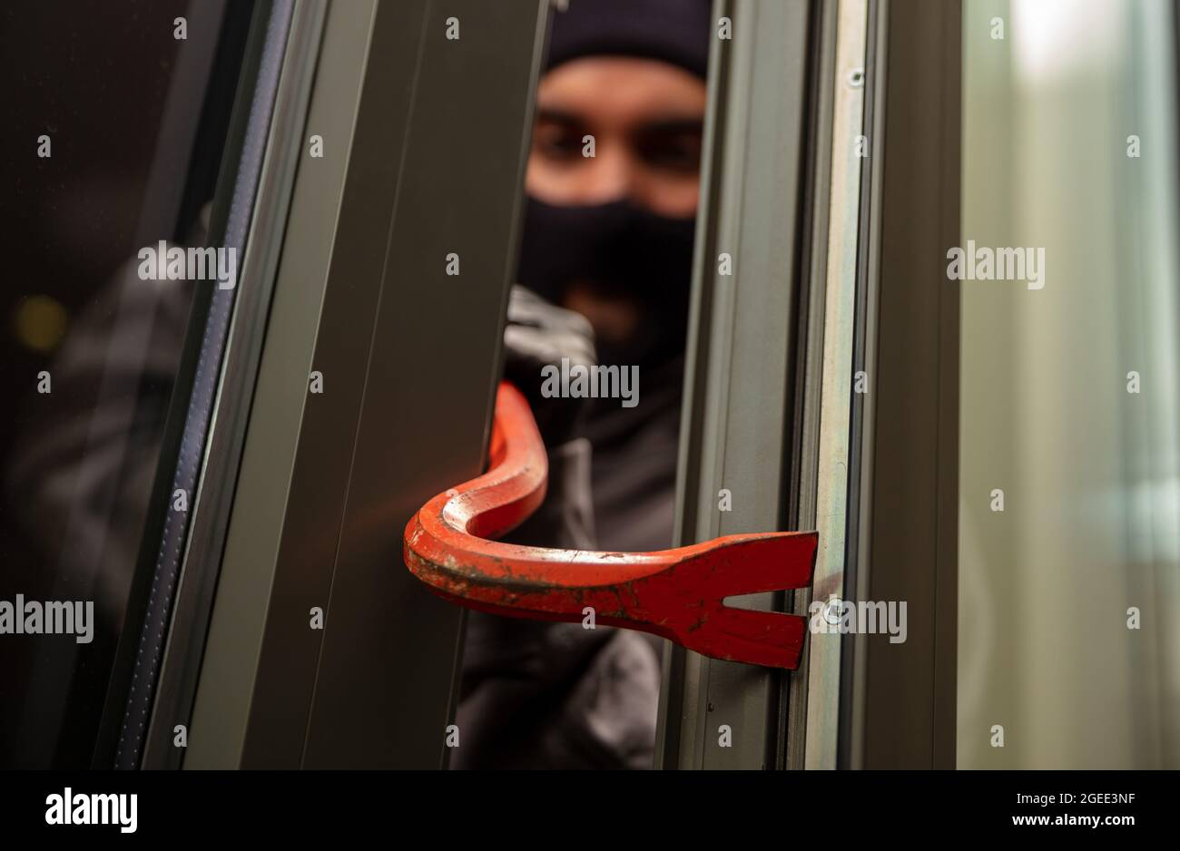 Housebreak with crowbar. Burglar in balaclava breaking a glass window ...