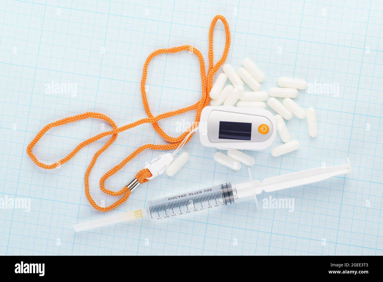 White pulse oximeter, capsules and syringe on graph paper background ...