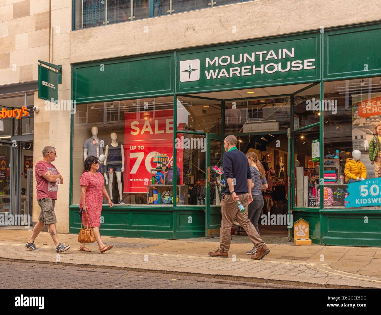 Pedestrians walk along the pavement of a city street. An outdoor store ...