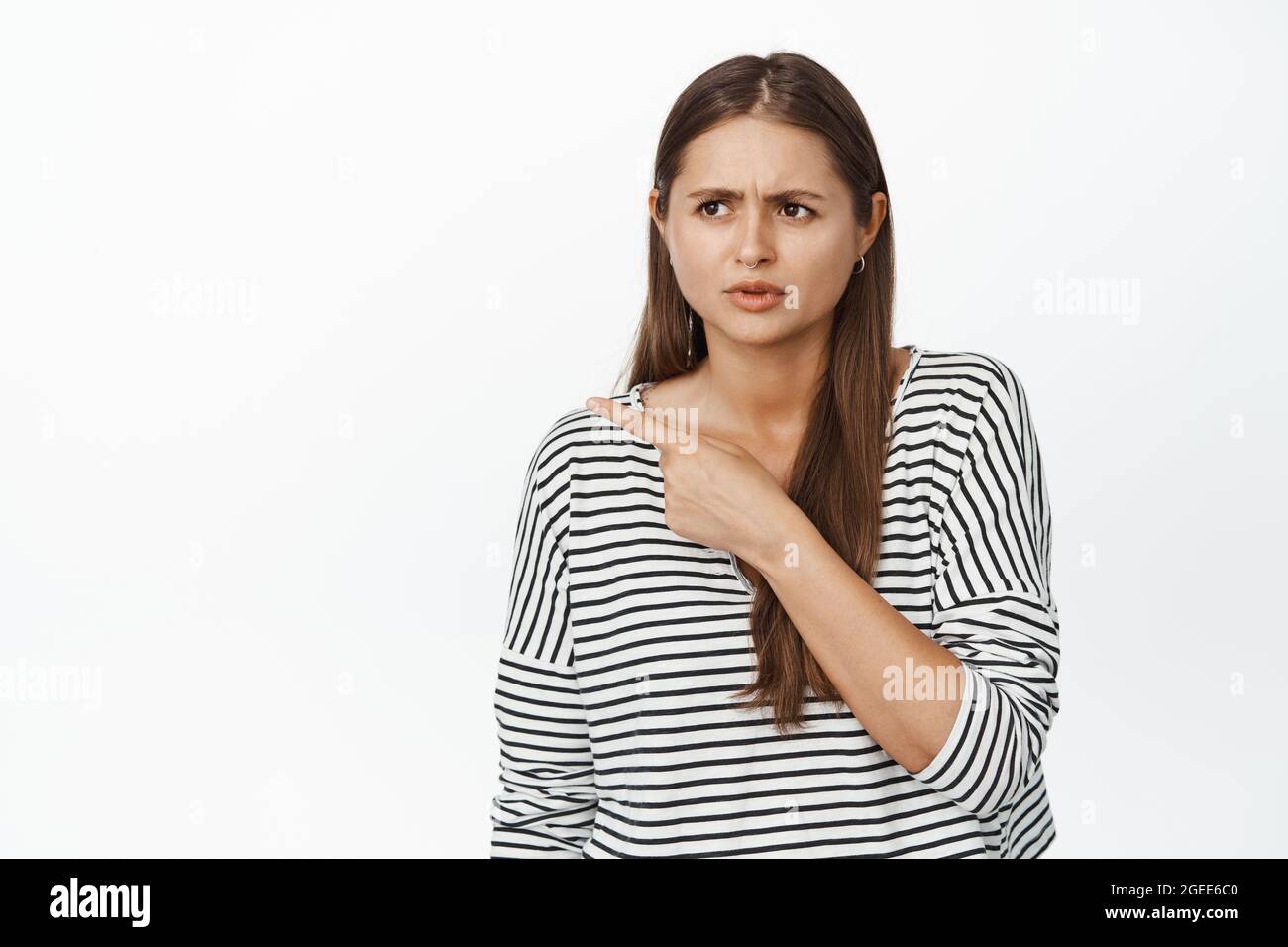 Confused girl pointing finger at upper left corner, looking with ...