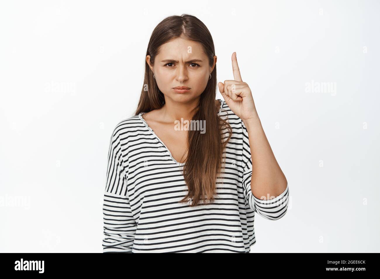 Frustrated young woman, frowning and pointing finger up at something ...