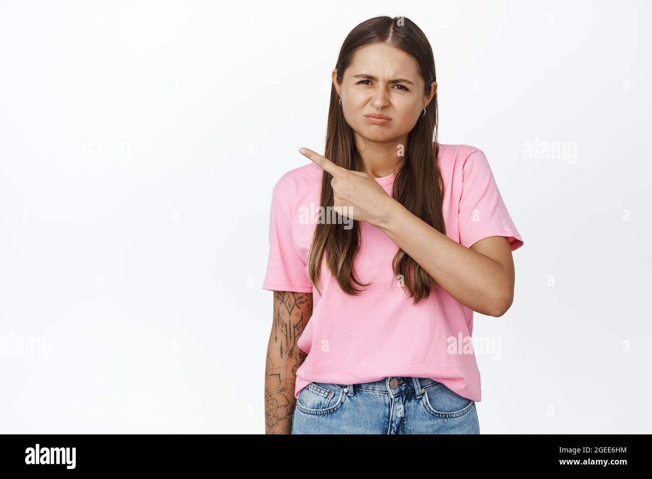 Sad and gloomy young woman pointing finger left and frowning ...
