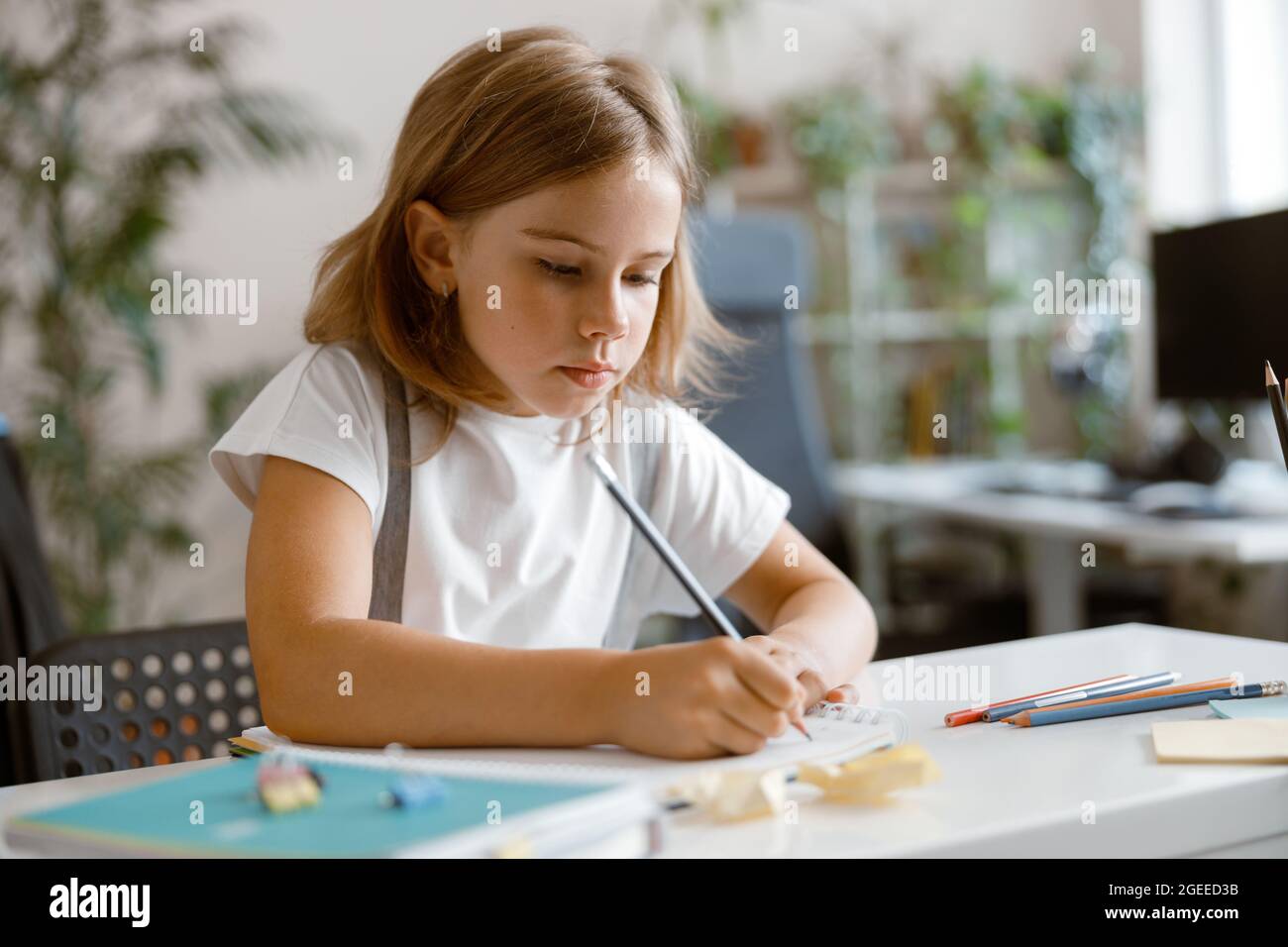 Little girl writes in notebook doing homework at desk in light room ...