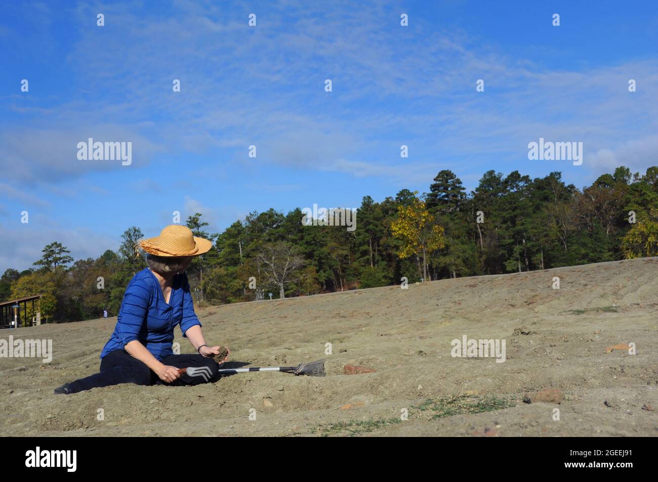 Woman, wearing a straw hat and holding a trowel, digs in the dirt at ...