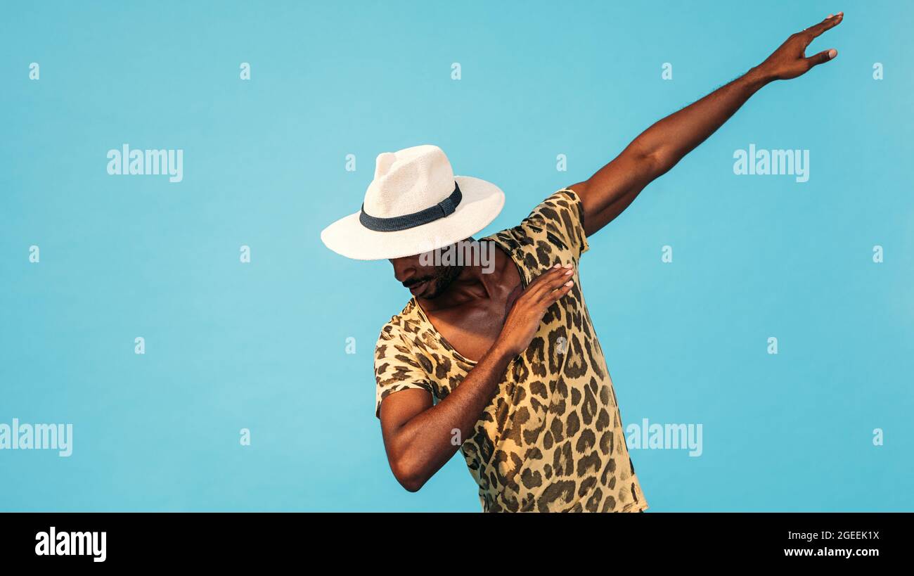 Young stylish guy in straw hat dancing in studio over blue background ...