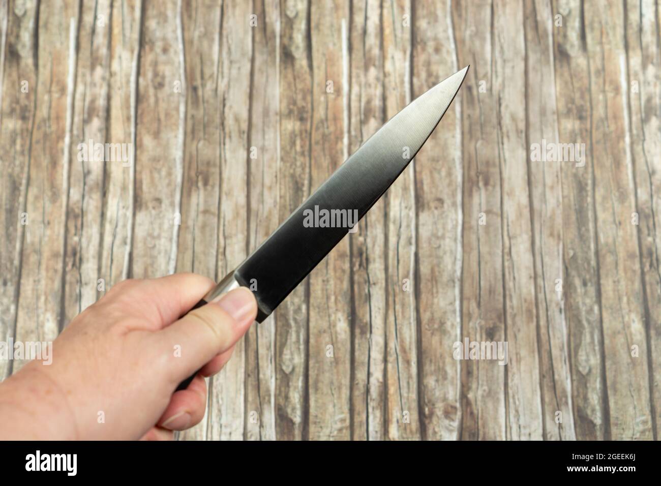 Man's hand holding a knife against wooden background Stock Photo - Alamy