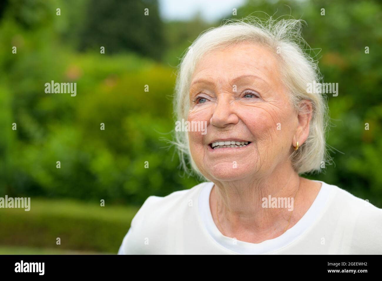 Smiling friendly 82 year old woman in her lush green garden looking ...