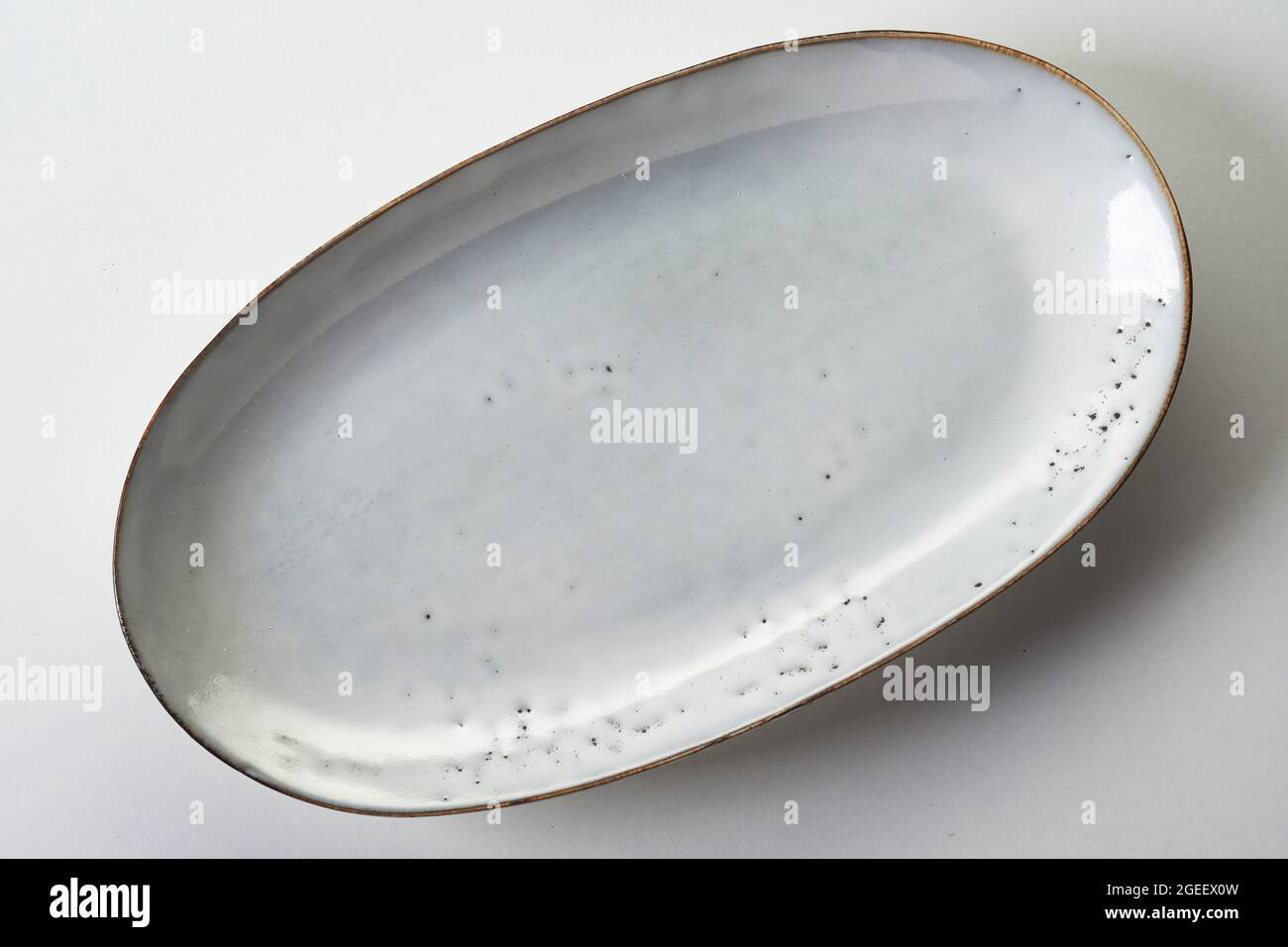 Oval-shaped white ceramic plate with a golden rim on white background ...