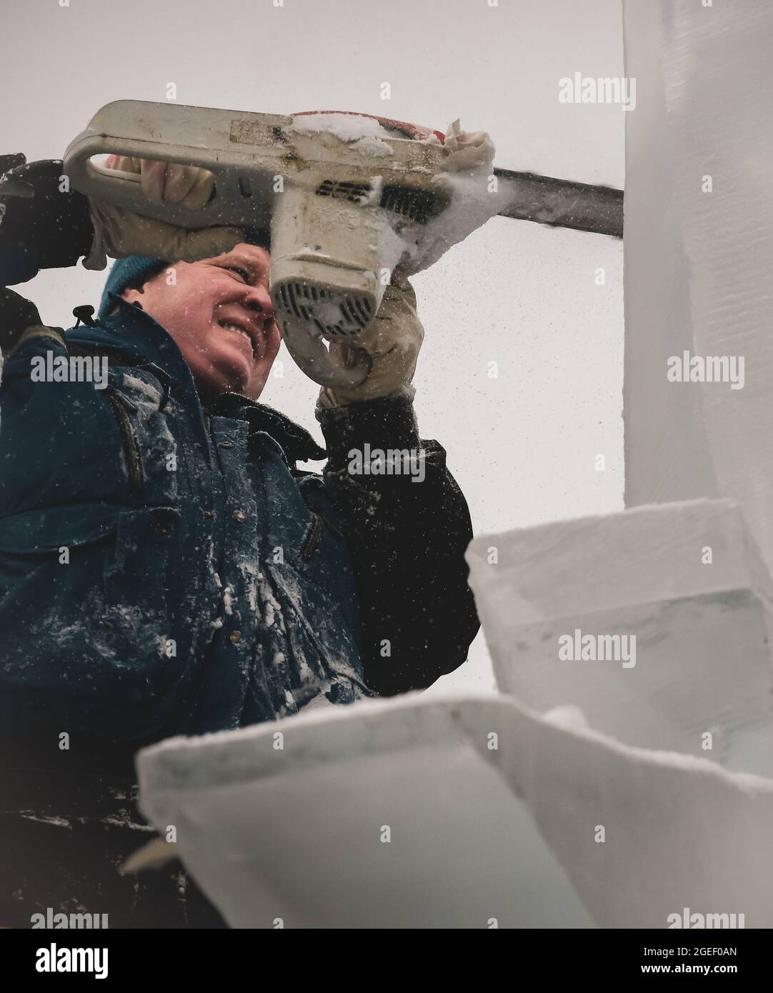 Professional ice carver sculpting block of ice with electric chainsaw ...
