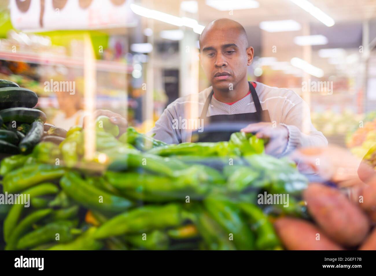 Merchandiser in an apron lays out ripe bell peppers on supermarket ...
