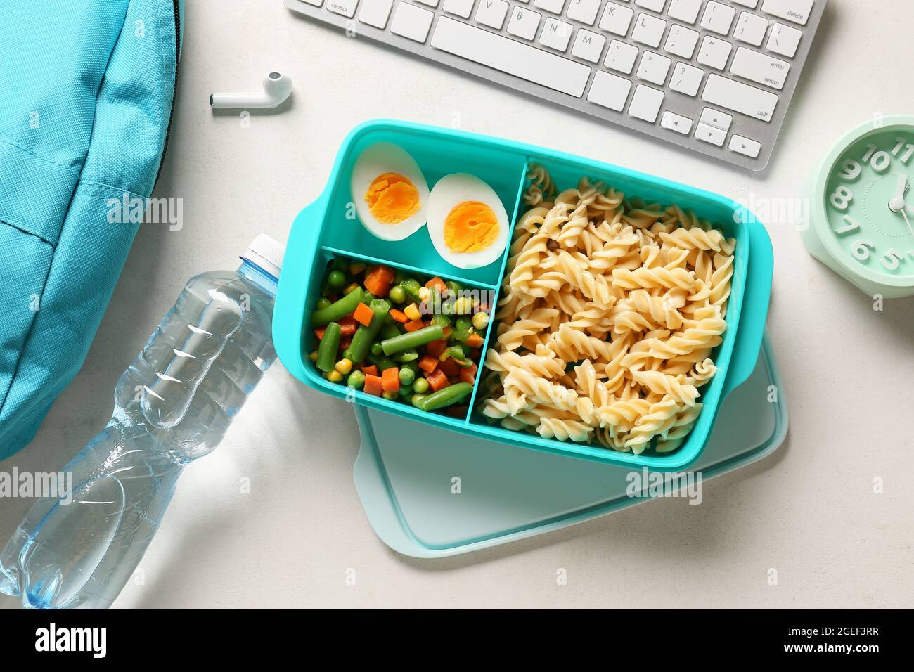 Lunch box with tasty food, bottle of water, alarm clock and keyboard on ...