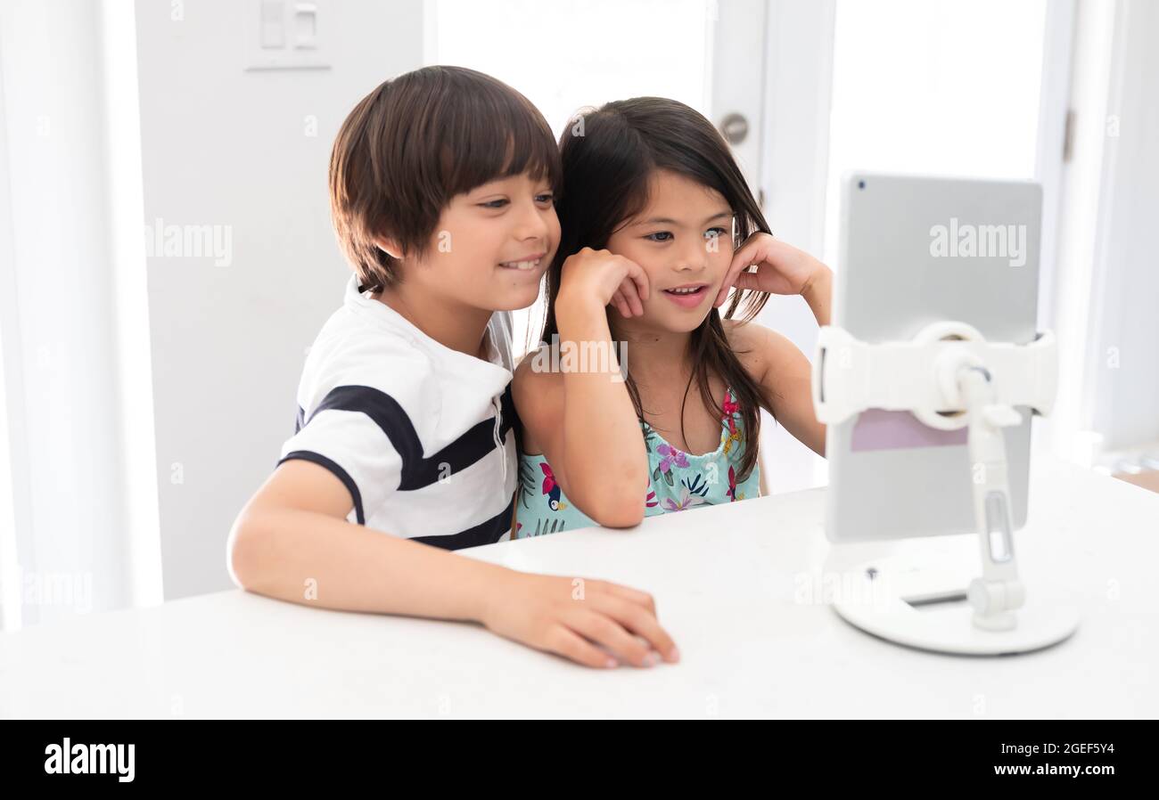 two biracial children smiling attending virtual online schooling at home during covid lockdown ...