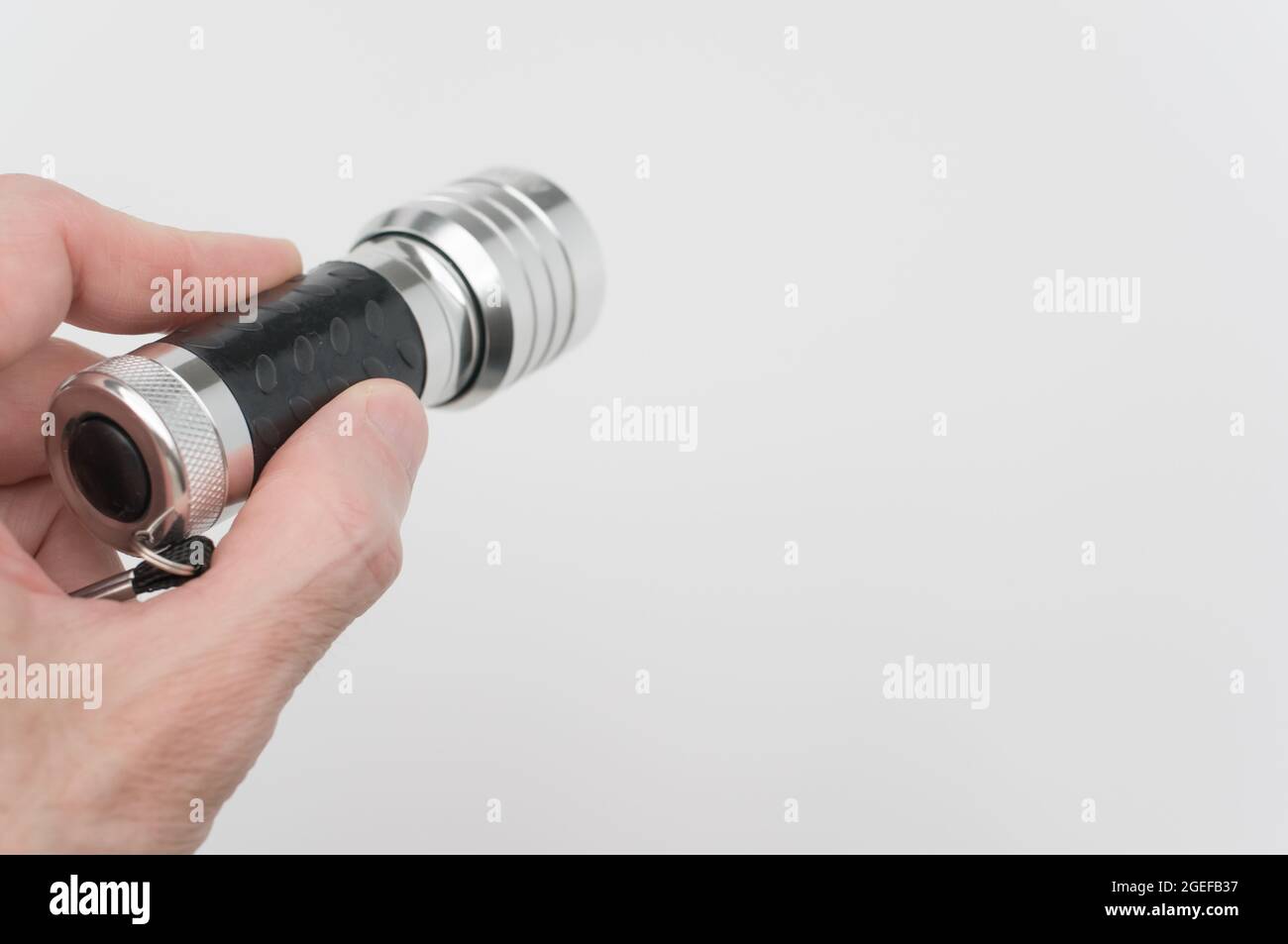 Hand of a male holding a small black-silver flashlight on a white ...