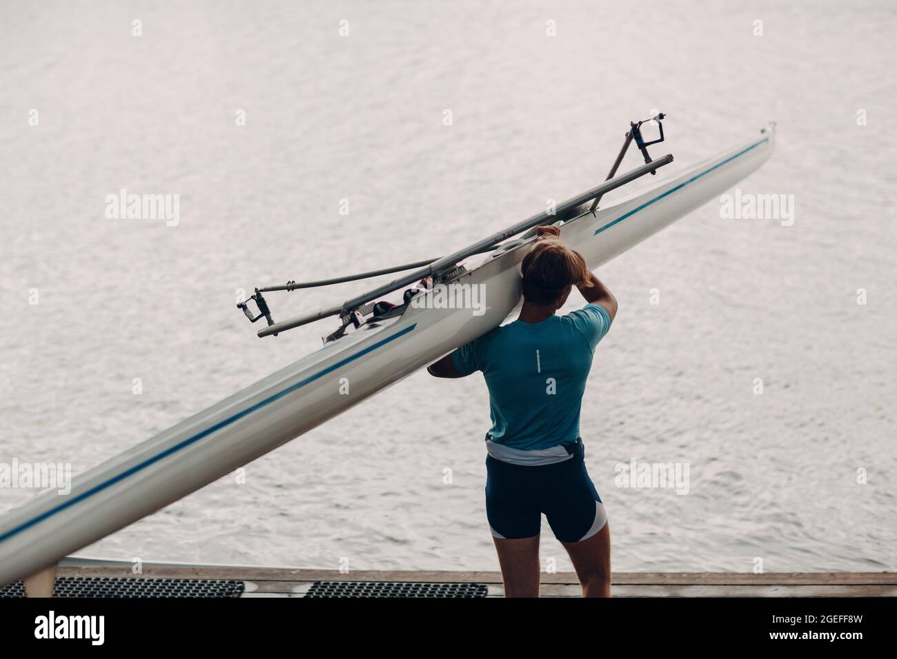 Sportsman single scull man rower carrying boat to competition on lake ...