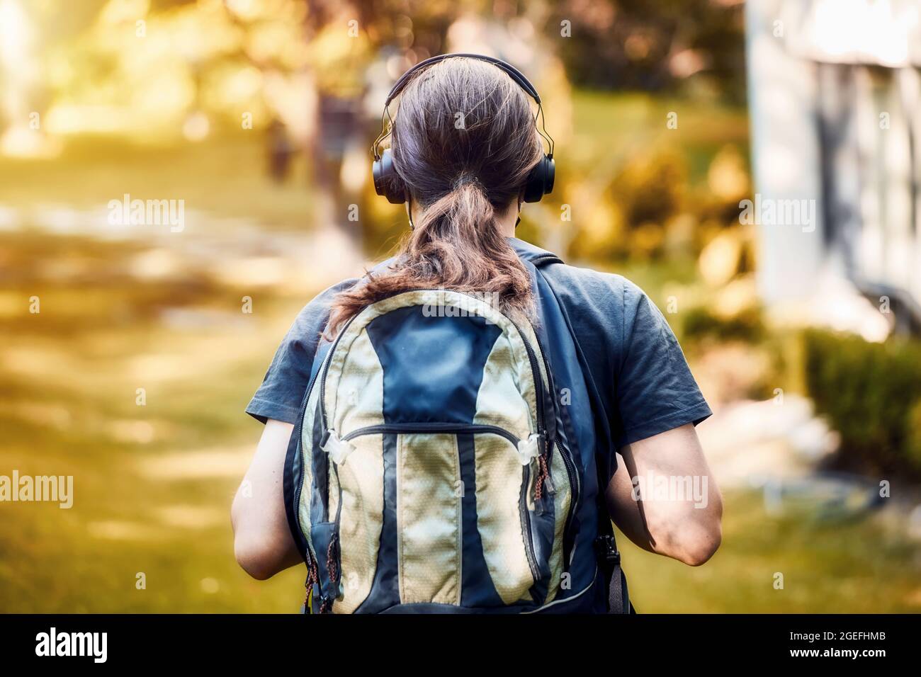 Facing back teenager high school boy with headphones and backpack walks ...