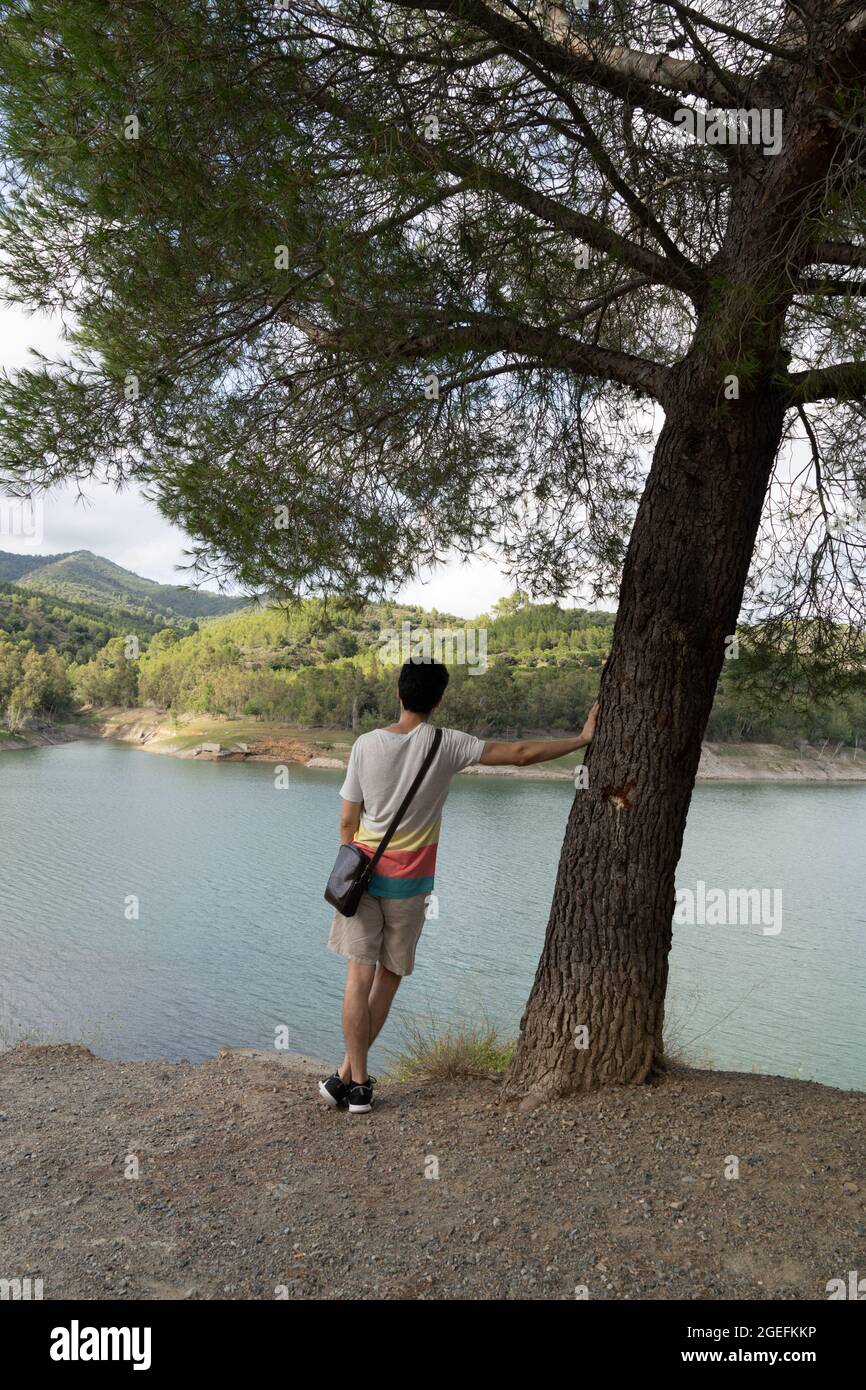 Vertical closeup of a young man leaning on the tree and looking at the ...