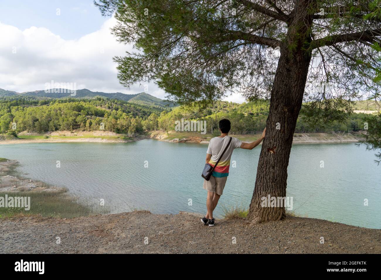 Closeup of a young man leaning on the tree and looking at the lake ...
