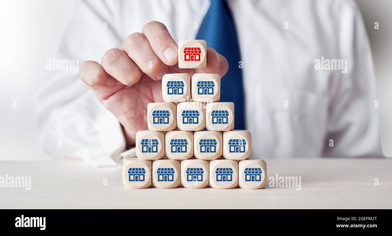 Businessman placing a cube with store icon on top of tiered wooden ...