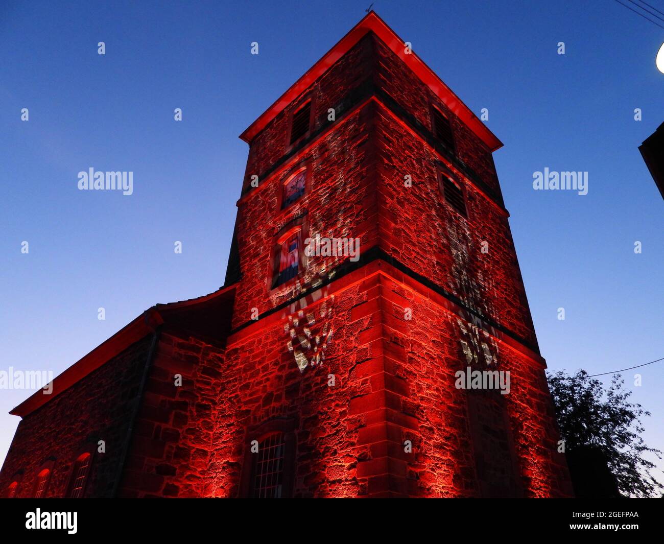Shot of a stone tower with a red color projection on it and a blue sky ...