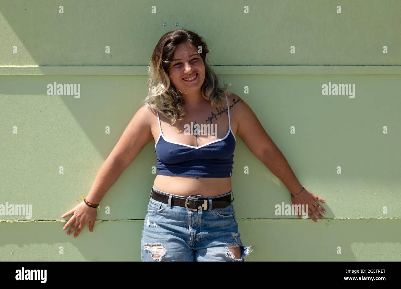 Portrait of happy Spanish girl laughing together against green wall ...