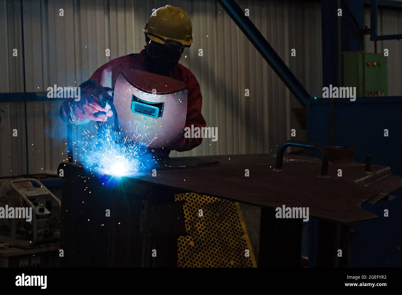A welder is using an electric arc welding machine in a fabrication ...