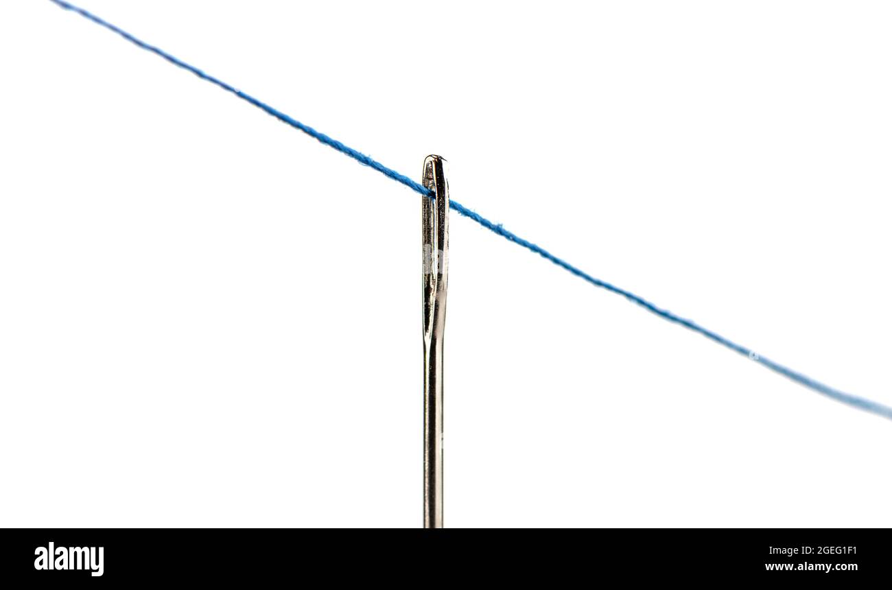 Stretched blue thread through the eye of a needle over a white ...